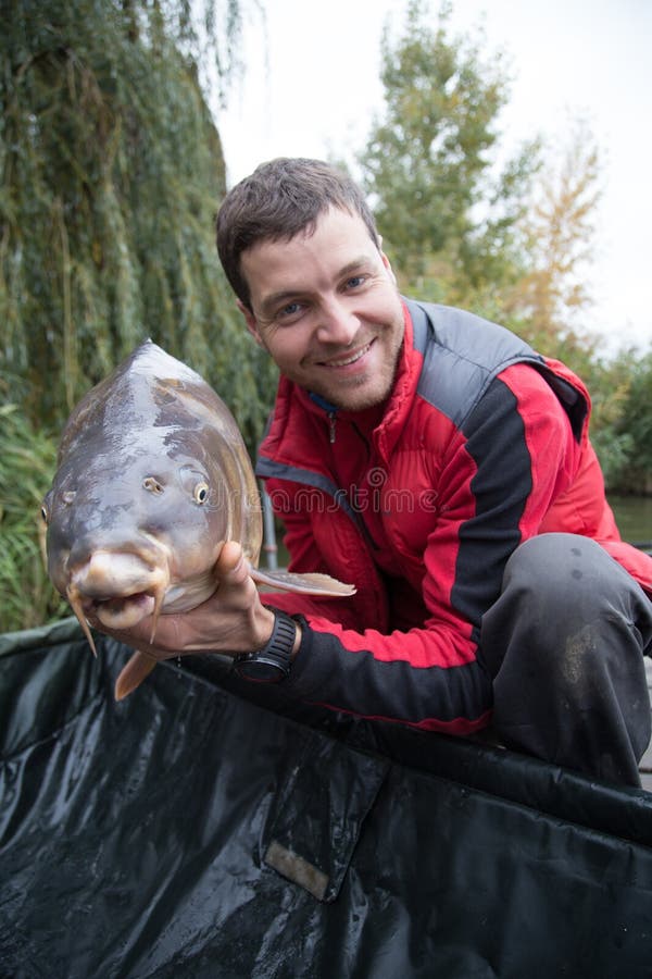 A Man is Photographed with a Large Carp Whom he Caught, Looking at the ...