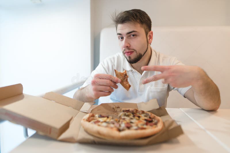 A Handsome Man with a Piece of Pizza in His Hands Poses on the Camera ...