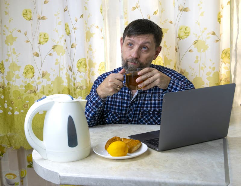 A Man in a Plaid Shirt is Drinking Tea at the Kitchen Table and Looking ...