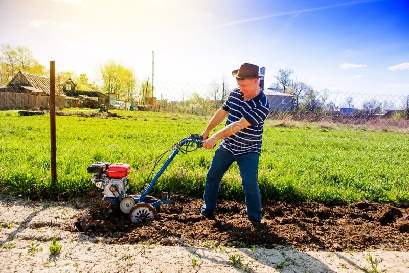 A Man Plows the Ground with a Tillerblock in the Garden Stock Photo ...
