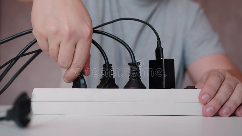 A Man Plugs Many Electrical Plugs with Wires into One Surge Protector ...