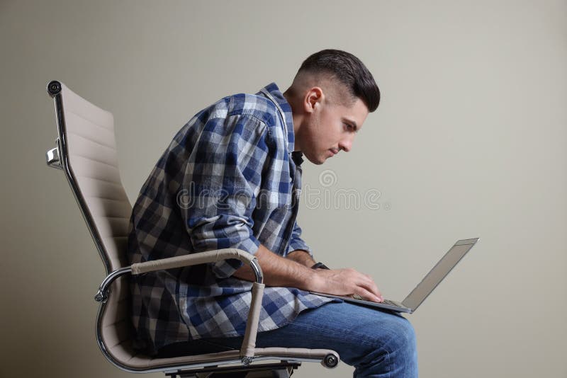 Man with Poor Posture Using Laptop while Sitting on Chair Against Grey ...