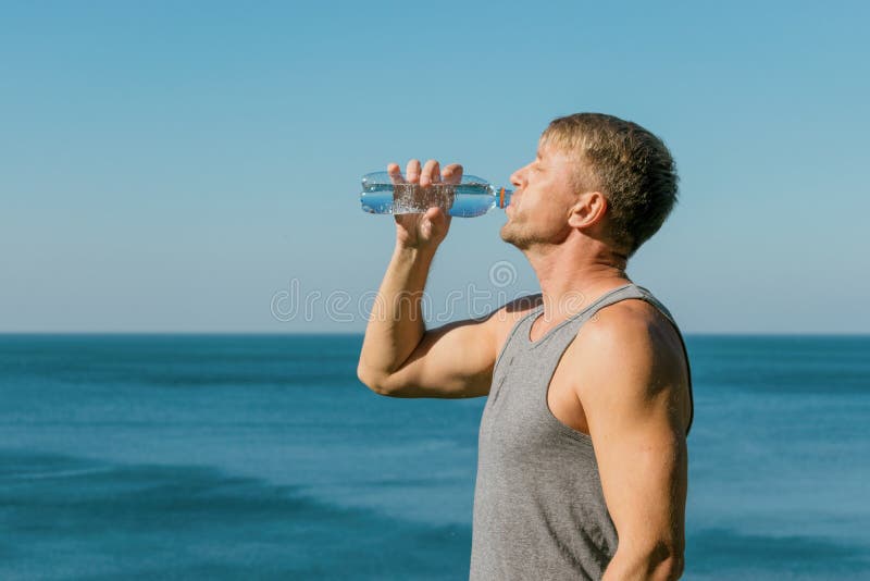 A Man Drinking and Pours Water on His Face from Bottle on the Ocean ...