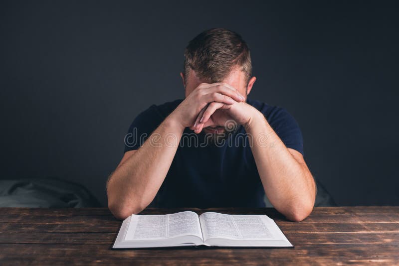A Man Prays with Folded Hands. an Open Holy Bible on the Table. a Young ...
