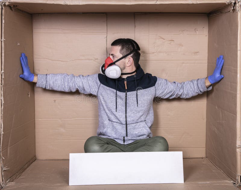 Man in a Protective Mask Sits by a Cardboard Box with His Hands To the ...