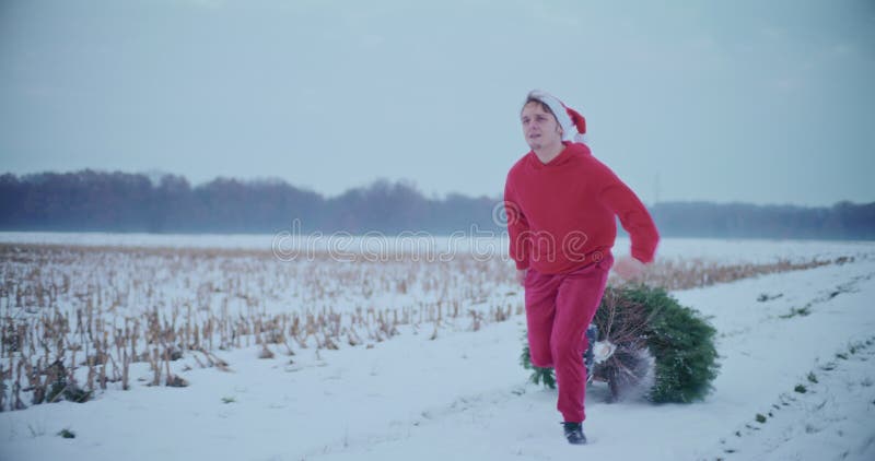 Man Pulling Christmas Tree while Running on Snow Covered Landscape ...