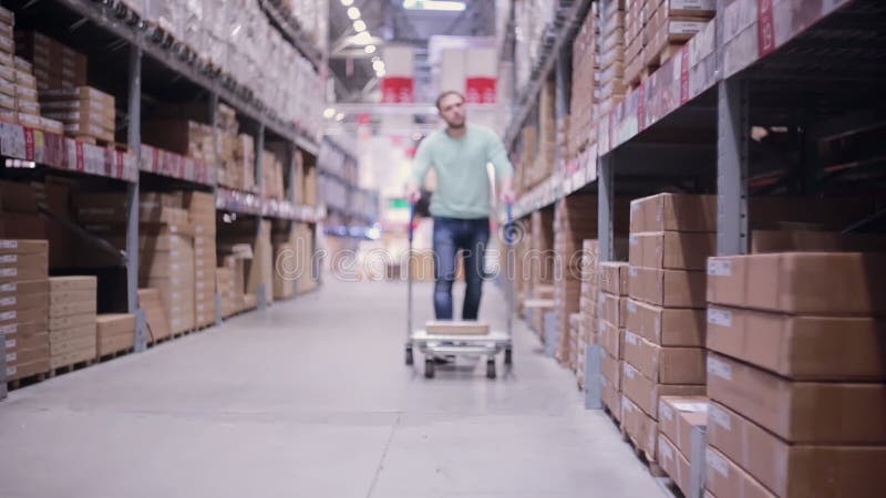 A Man Pushing a Trolley in a Storage Warehouse is Moving into the ...