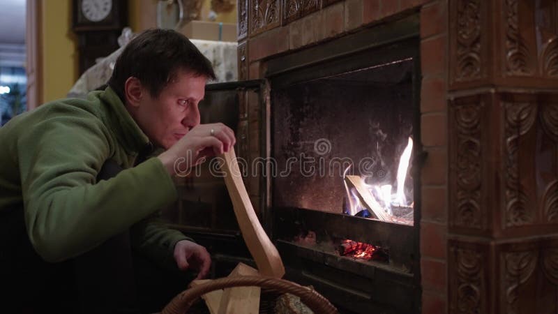 A Man Putting Firewood into a Fireplace, Keeps a Fire Burning Stock ... A Man Putting Firewood into a Fireplace, Keeps a Fire Burning Stock ...