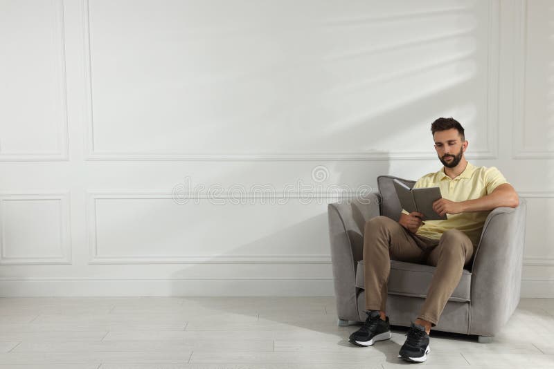 Man Reading Book in Armchair Near White Wall, Space for Text Stock ...