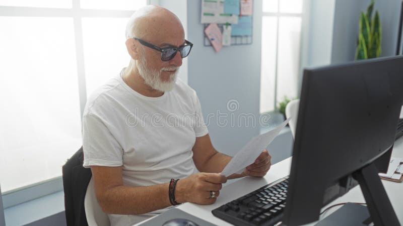 Man Reading Documents at a Desk in a Modern Office with a Computer ...