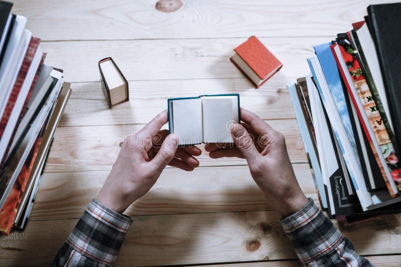 A Man Reading a Miniature Book among the Big Books in the Library Stock ...