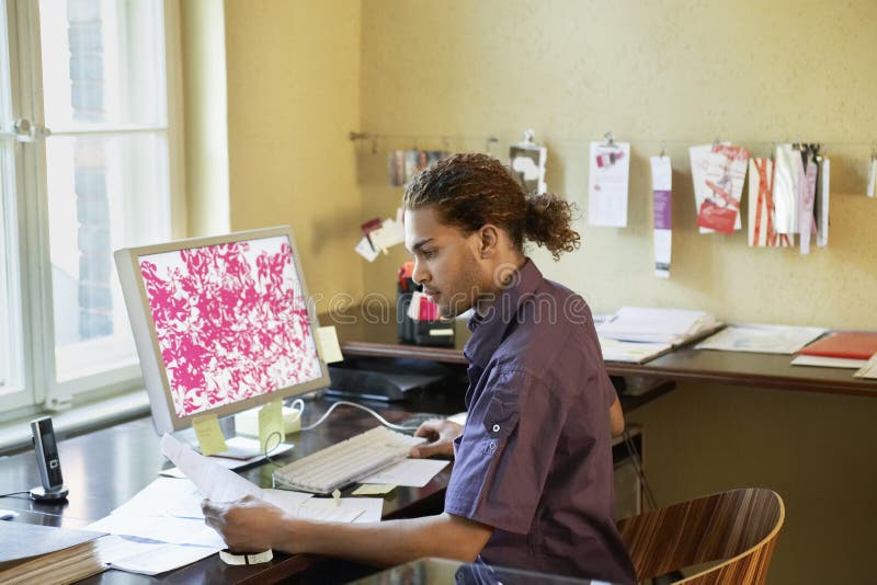 Man Reading Papers by Computer in Office Stock Photo - Image of flat ...