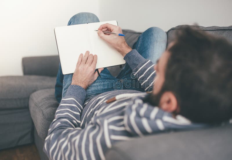 Man Relaxing on Sofa while Taking Notes or Writing in Diary or Notebook ...