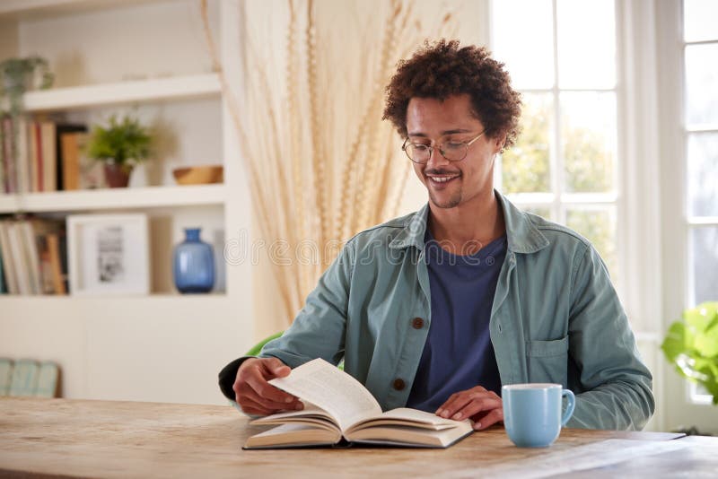 Man Relaxing at Home Sitting at Table Reading Book with Hot Drink Stock ...