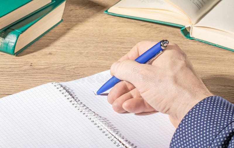 A Man& X27;s Hand with a Blue Pen Makes Notes in an Open Notebook on an ...