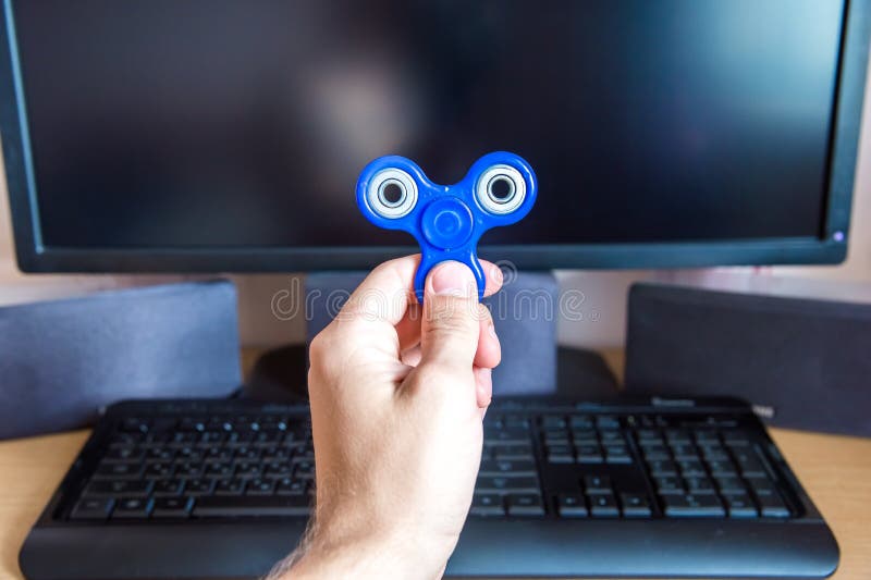 Man`s Hand Holds a Spinner on the Background of a Personal Computer ...