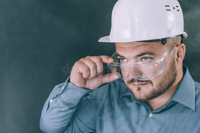 A Man in Safety Glasses and a Construction Helmet on a Dark Background ...
