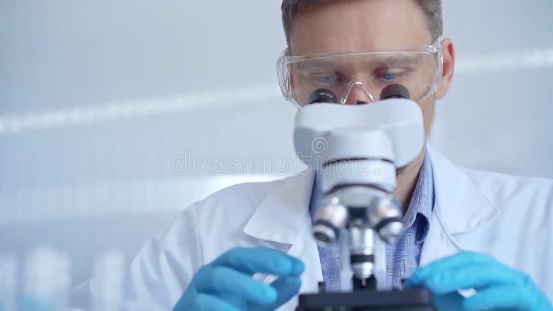 Man Scientist with Protective Glasses and Gloves is Using Microscope in ...