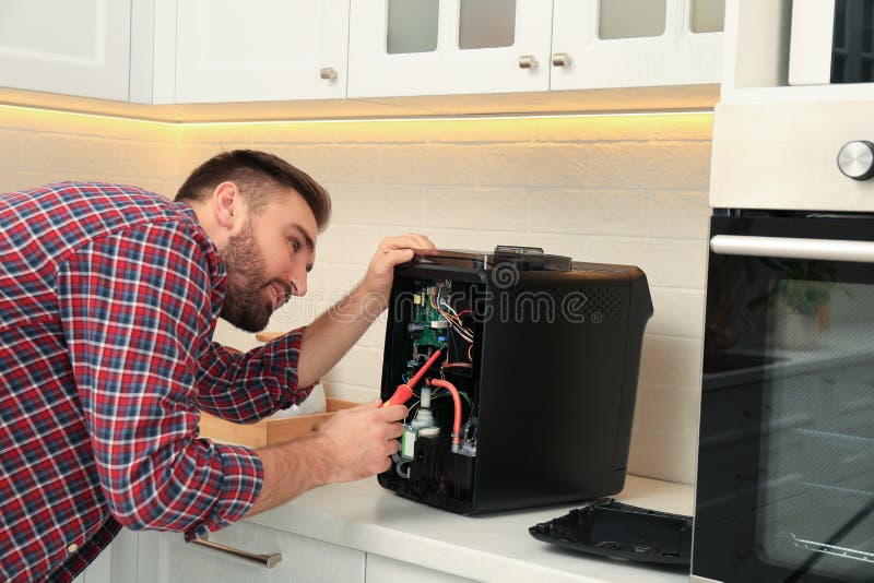 Man with Screwdriver Fixing Coffee Machine at Table in Kitchen Stock ...