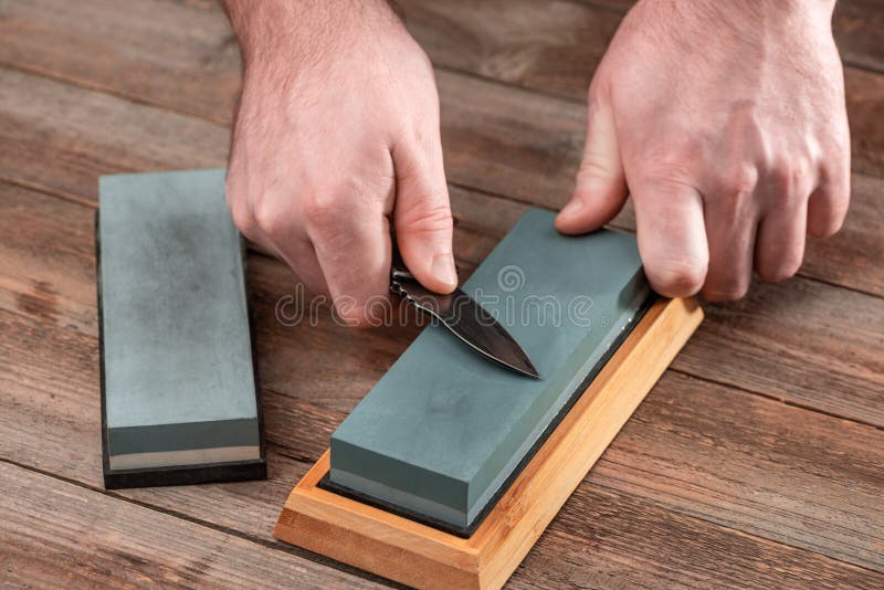 Man Sharpening His Jackknife with a Whetstone on a Rustic Wooden Table ...