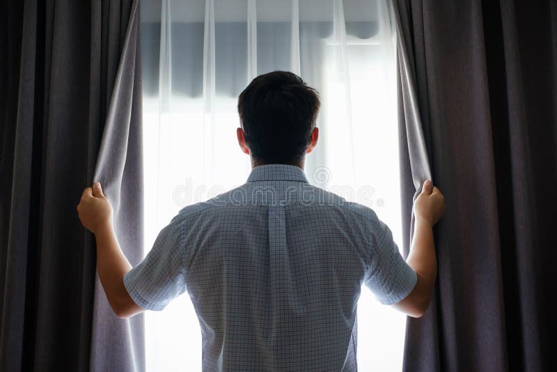 Man in Shirt Stands at Window and Opens Curtains, Back View. Stock ...