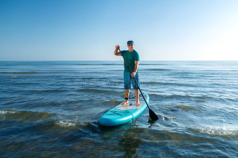 A Man In Shorts Stands On A Sup Board In The Evening At Sunset In The