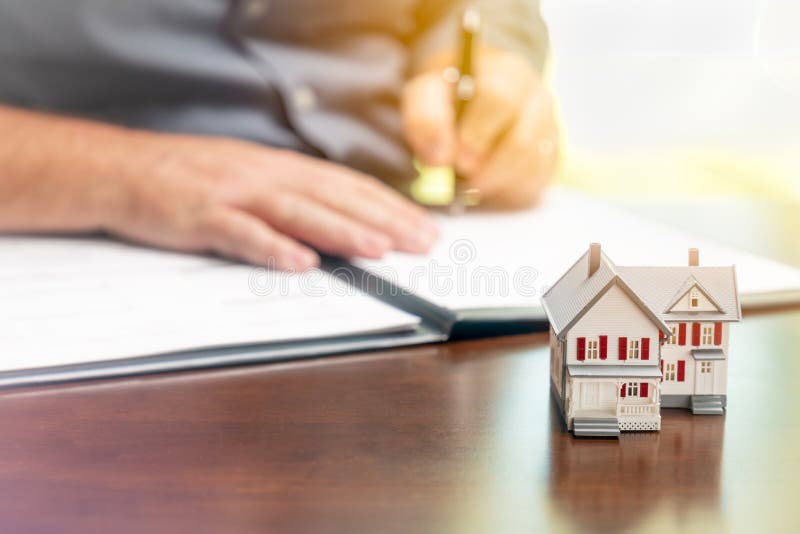 Man Signing Real Estate Contract Papers with Small Model Home in Front ...