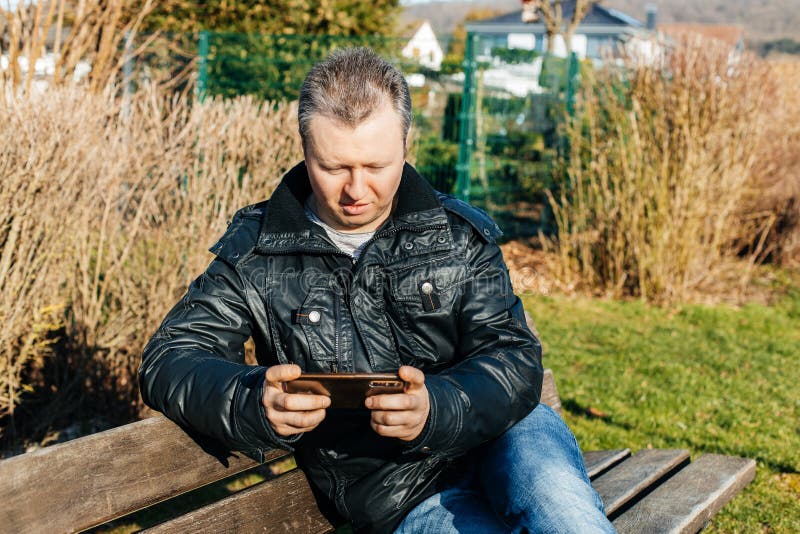 A Man Sits on a Bench and Uses a Mobile Phone. Wireless Technologies ...