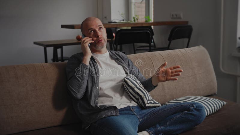 A Man Sits Comfortably on a Sofa, Talking on the Phone with a Cheerful ...