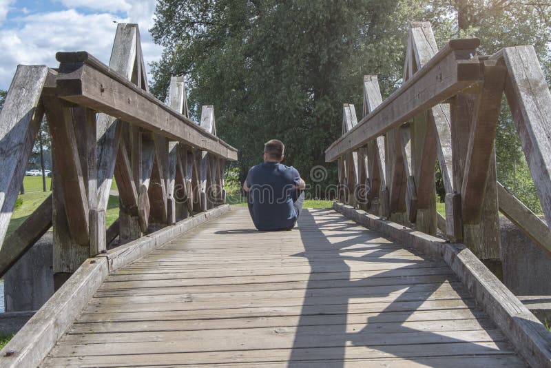 The Man Sits with His Back Turned on an Old Wooden Bridge Stock Image ...