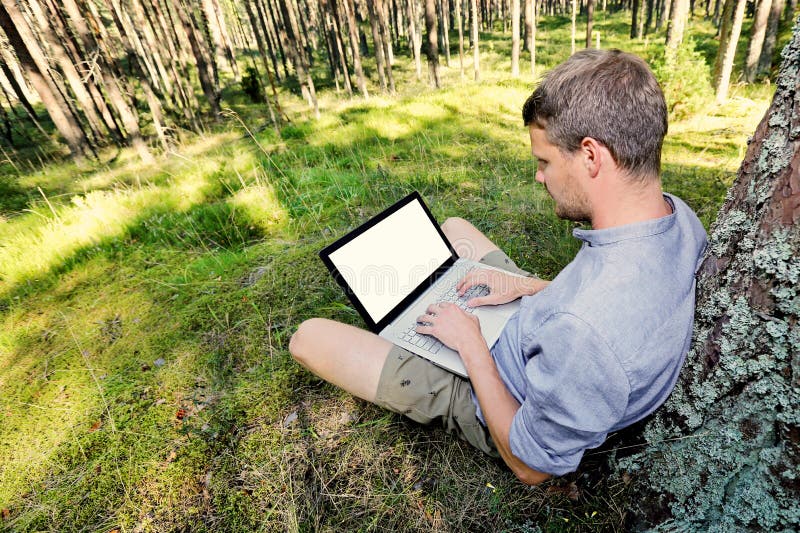 Man is Sitting Against a Tree in the Forest, Working with His La Stock ...
