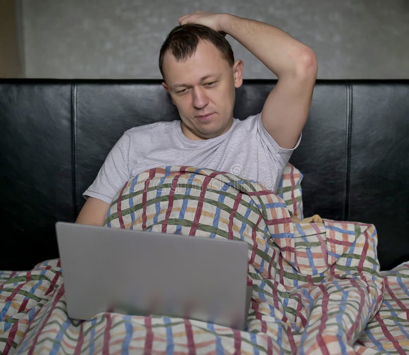 Young Man Sitting in Bed Under the Covers with a Laptop Stock Photo ...