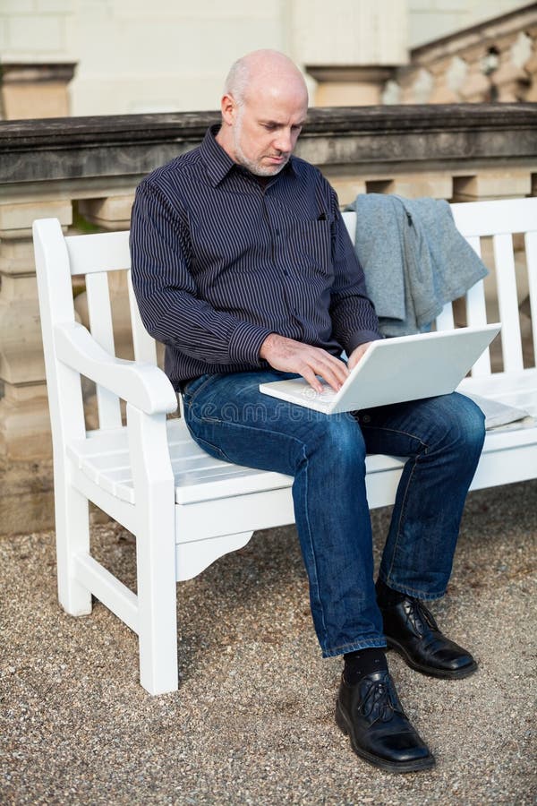 Man Sitting on a Bench Using a Laptop Stock Image - Image of bench ...