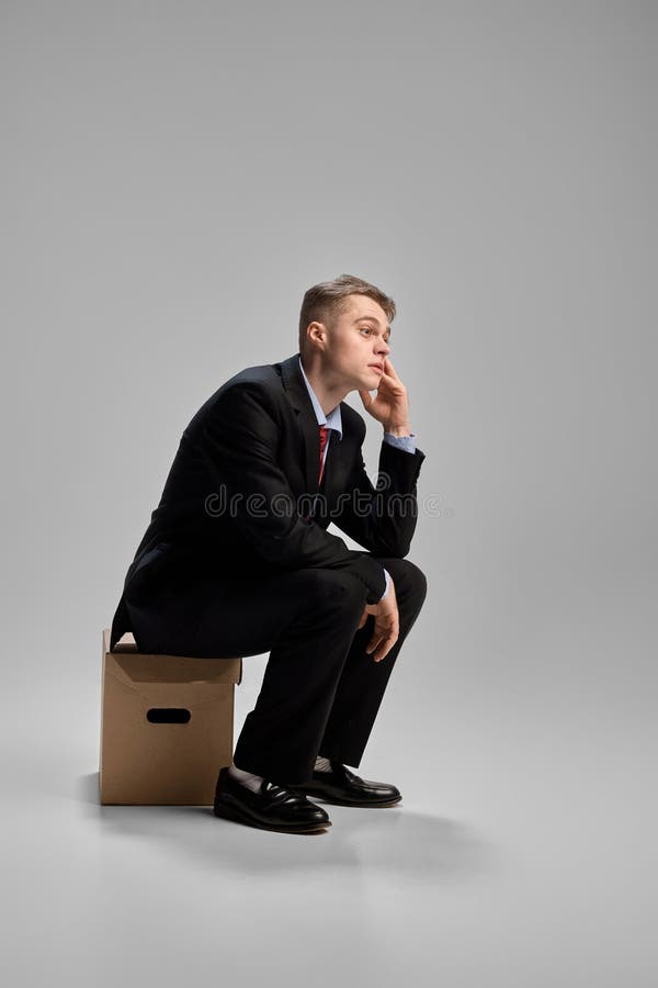 Man Sitting on Box, Leaning Forward, Resting Chin on Hand, Appearing ...