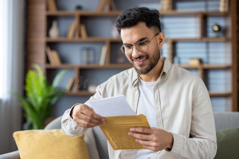 Smiling Man Opening Envelope at Home, Experiencing Joy and Anticipation ...