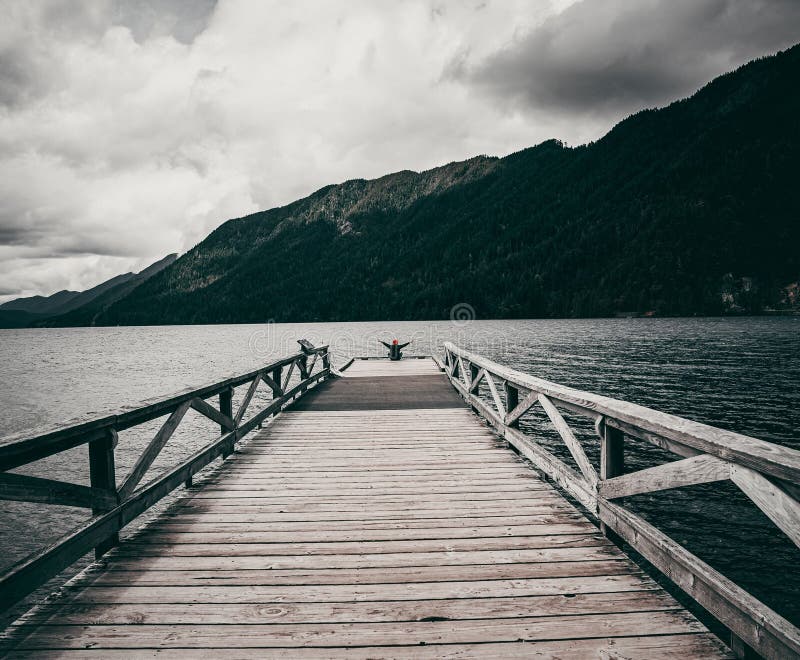 Man Sitting on the Edge of the Dock with a View of a Lake and the ...