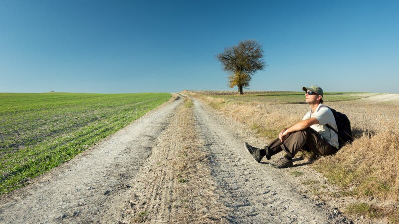 A Man Sitting by the Road, Fields and a Lonely Tree Stock Photo - Image ...
