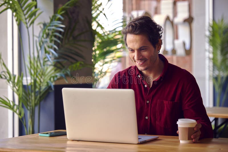 Man Sitting at Table in Coffee Shop Working on Laptop Computer Stock ...
