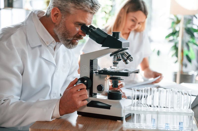 Man is Sitting and Using Microscope. Two Clinic Workers are Indoors ...