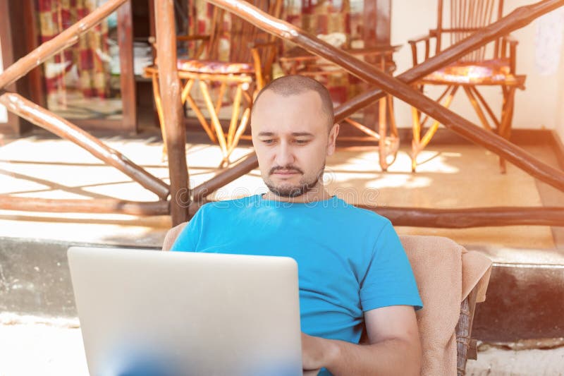 A Man Sitting on a Wicker Lounge Chair and Working at the Computer. the ...