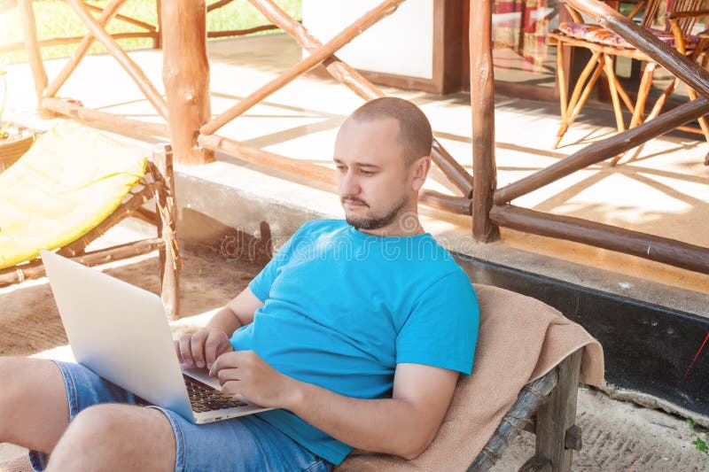A Man Sitting on a Wicker Lounge Chair and Working at the Computer. the ...