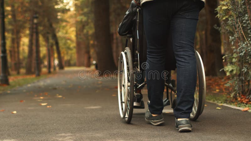 Man Slowly Rolling a Wheelchair with a Disabled Man on the Path in the ...