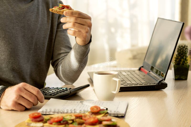 Man Snacking on Sandwich and Coffee while Working at Table in Office ...