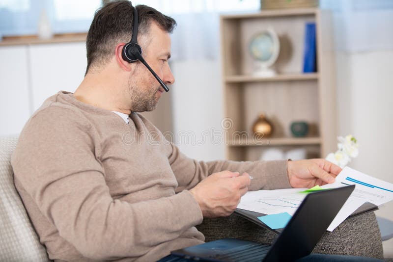 Man on Sofa Looking at Paperwork and Wearing Headset Stock Image ...