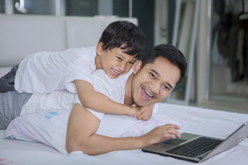 Man and Son Laughing while Using Laptop on Bed Stock Image - Image of ...