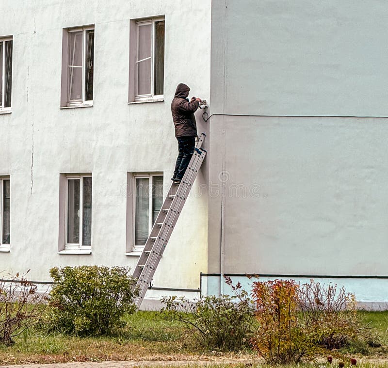 A Man on the Stairs Installs a CCTV Camera on the Wall of the House ...