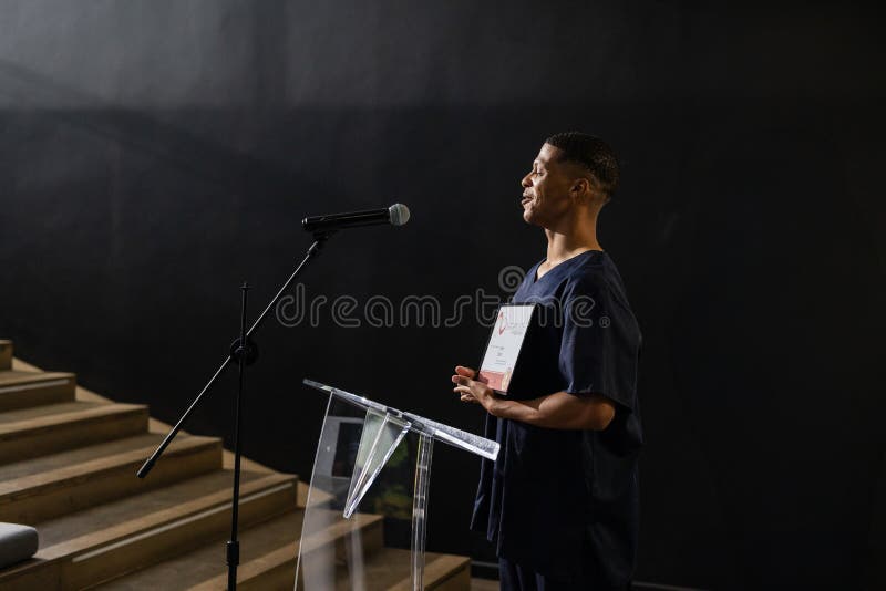 Man Standing beside Acrylic Lectern Holding Certificate, Using Mic on ...