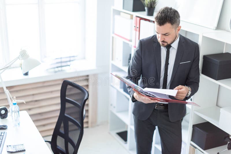The Man is Standing Near the Rack in the Office and Scrolls through the ...