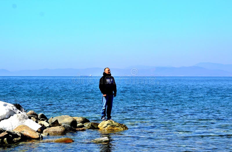 A Man Standing on the Rocks Against the Backdrop of the Sea and Looking ...