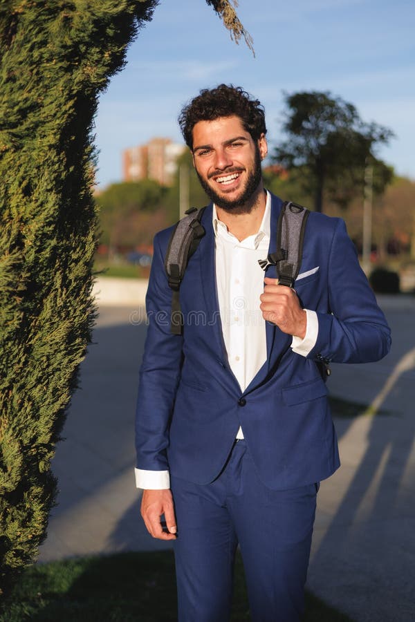 A Man in a Suit with a Backpack Stands Next To a Tree, Smiling Happily ...